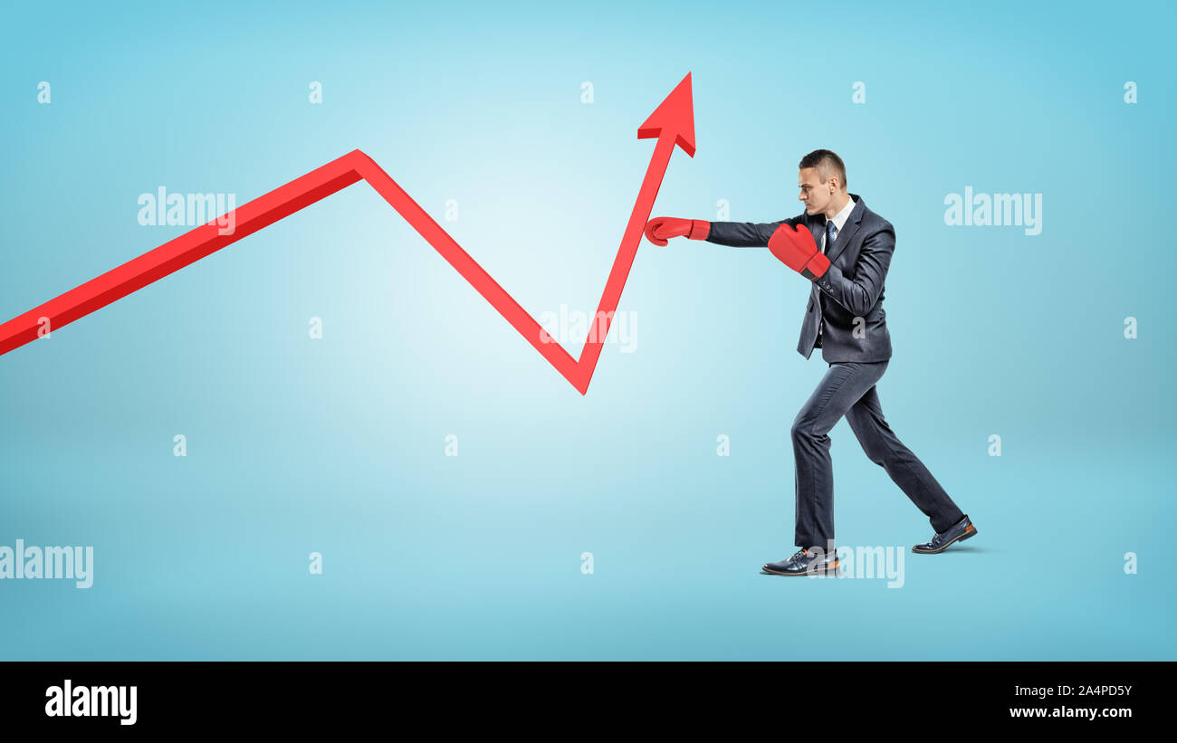 A businessman in red boxing gloves punches a red statistic arrowed line ...