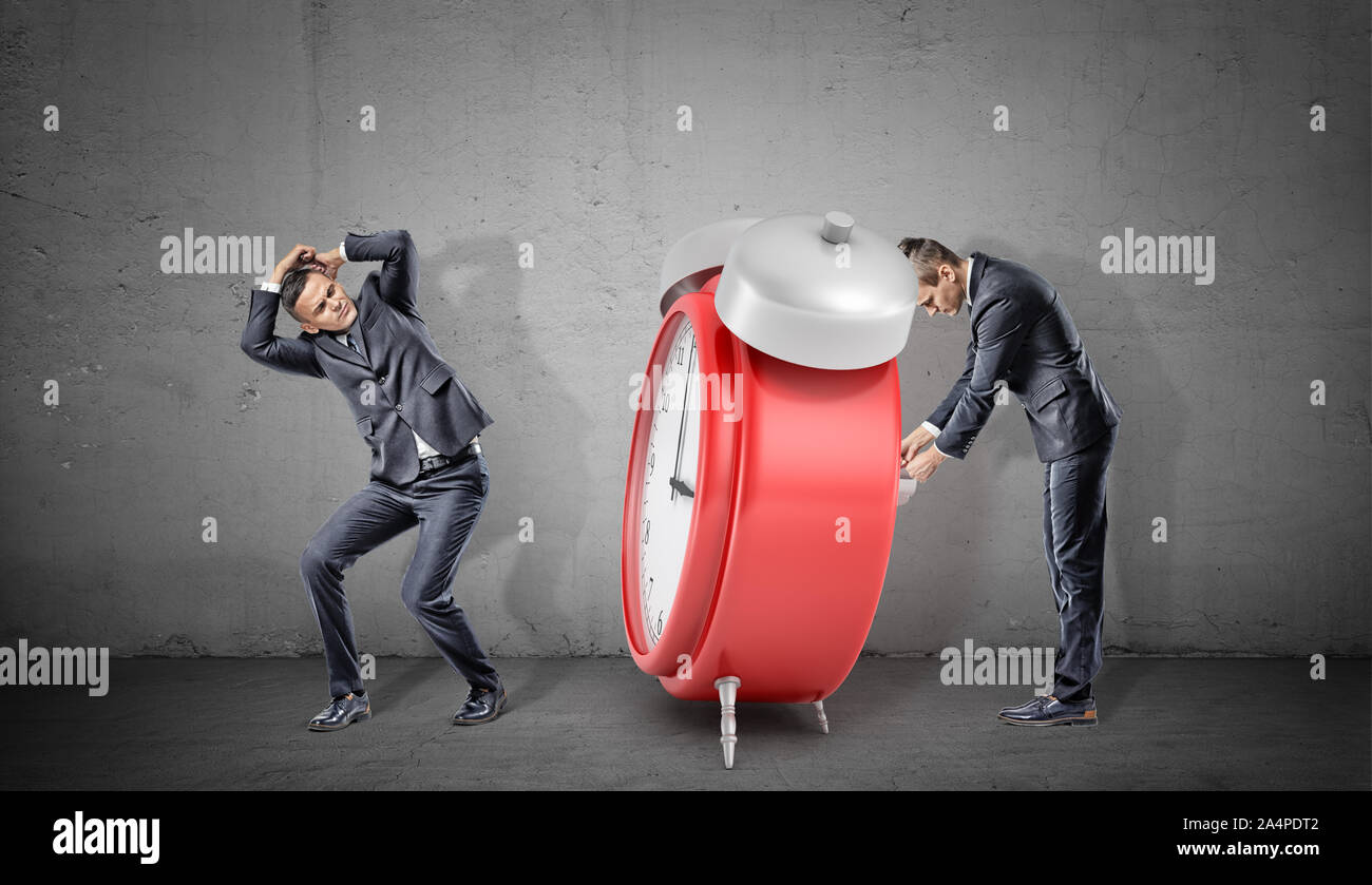 A businessman covers his head form a giant red retro alarm clock being ...