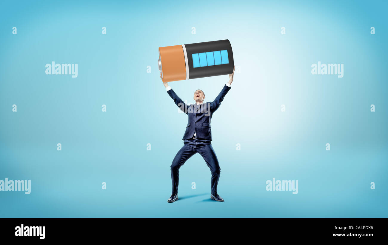 A small happy businessman smiles and holds a huge fully charged battery ...