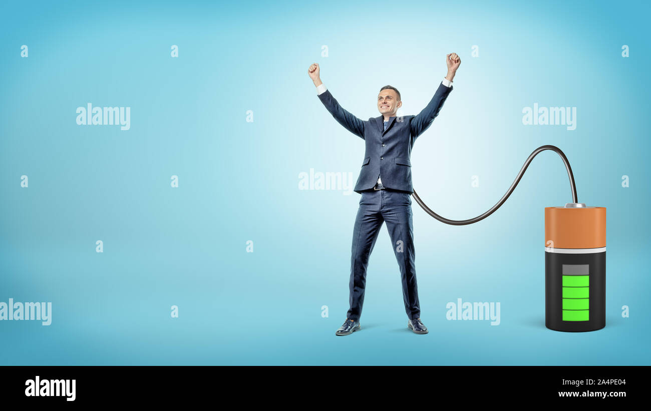 A happy businessman with raised hands is connected to a large battery ...