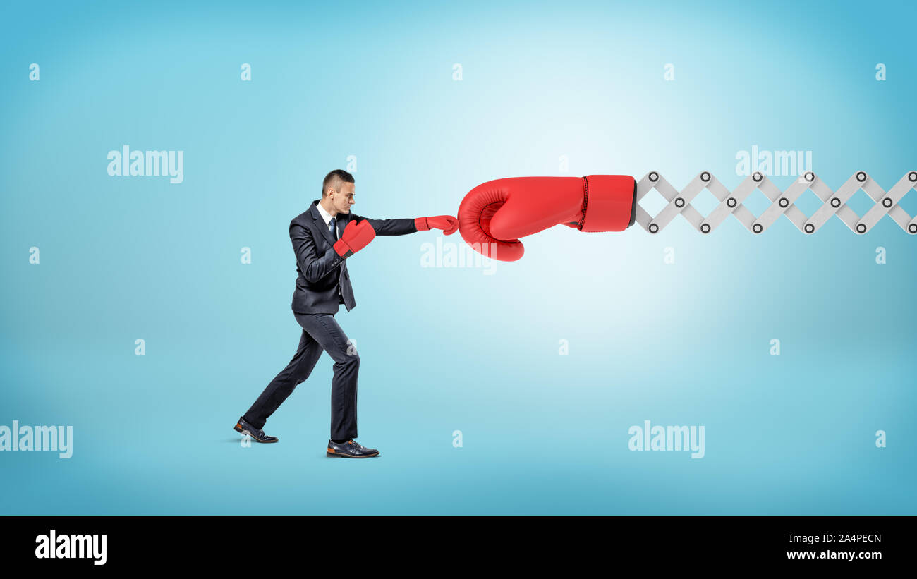 A small businessman in sport gloves punches a giant red boxing glove on ...