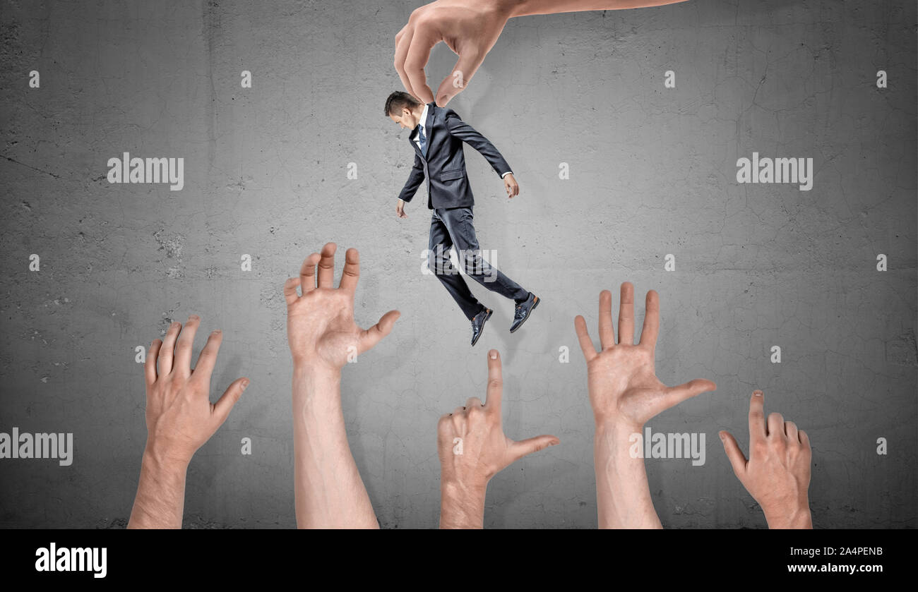 A giant hand holds a small businessman over many giant grabbing hands ...