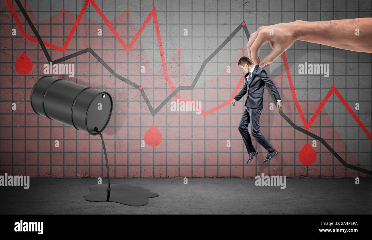 A small businessman caught by a giant male hand over a spilling oil ...