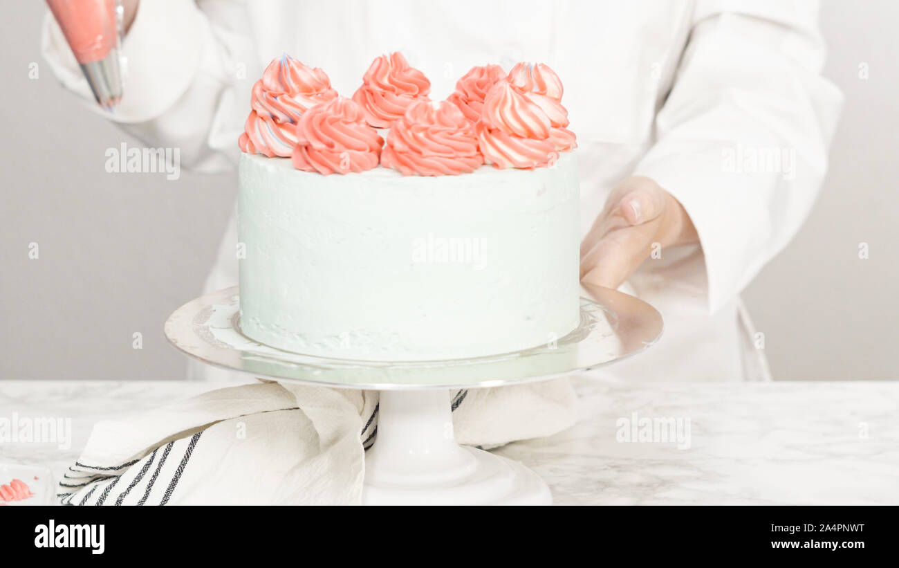 Piping buttercream rosettes on top of round three-layer vanilla cake ...