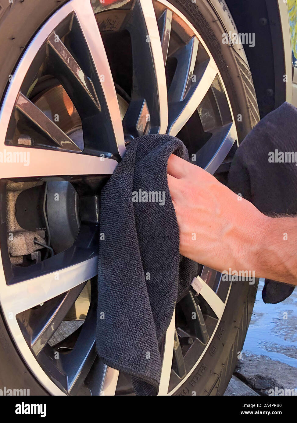 Man's hand cleaning wheel and tire with black microfiber cloth. Hand ...