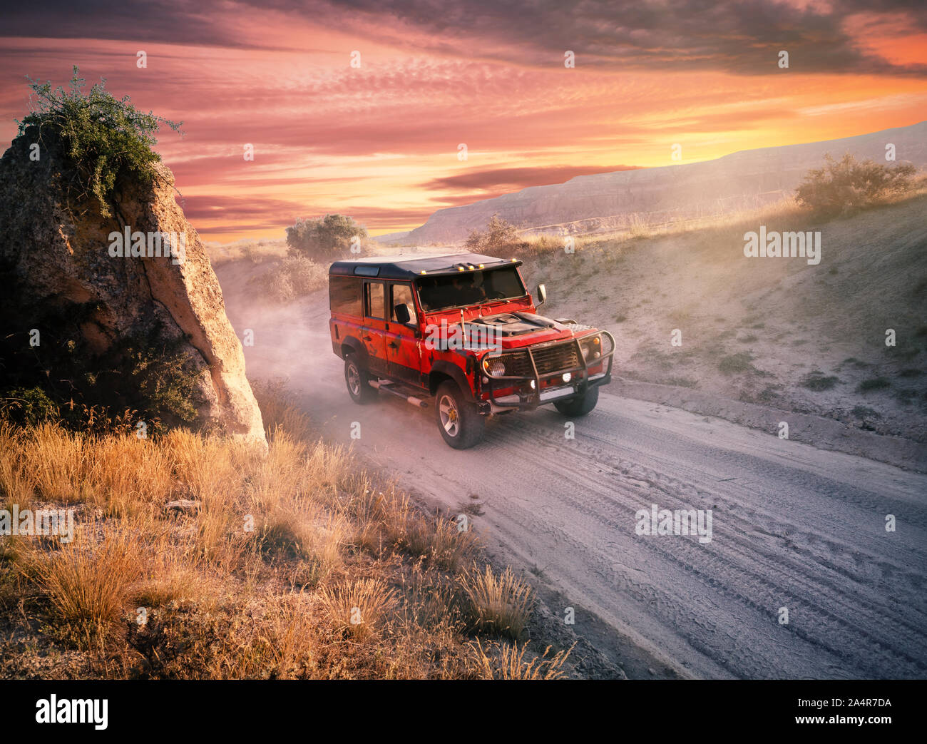 Red off-road car on a dusty road. Dramatic sunset sky. Trademark ...