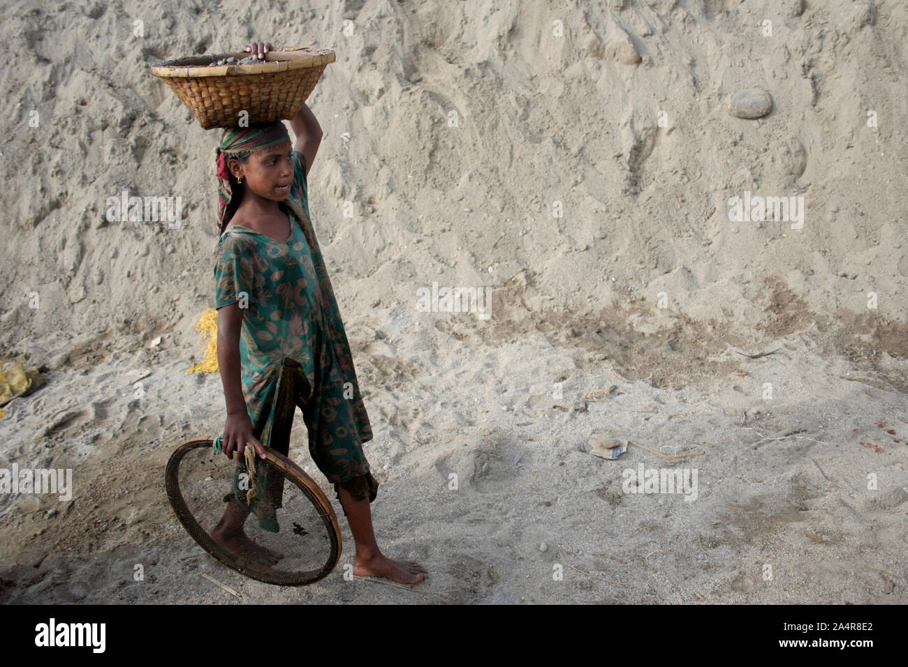 A young girl carries stones and pebbles collected from a stone quarry ...