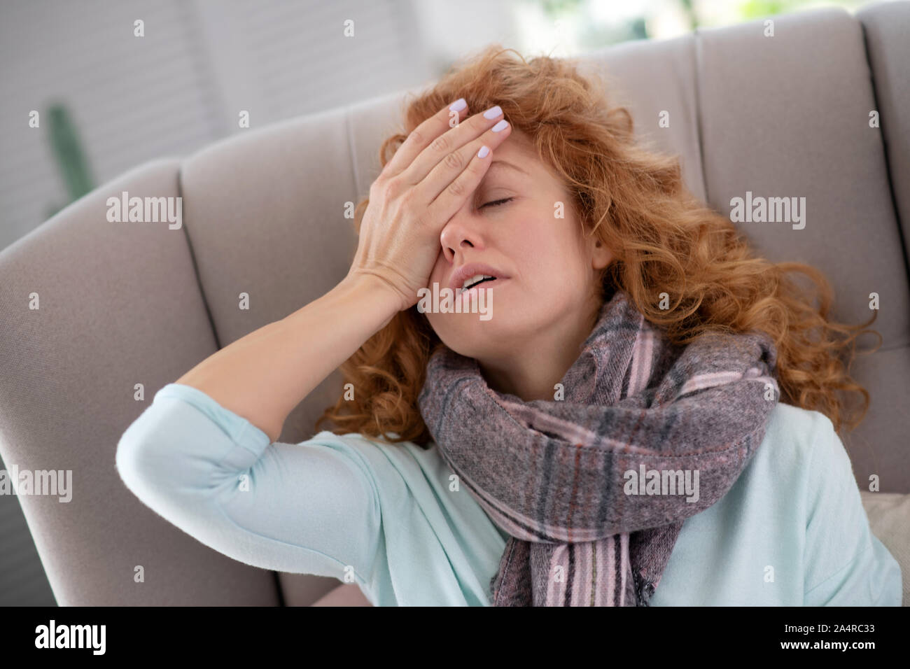 Red-haired woman touching forehead while checking temperature Stock ...