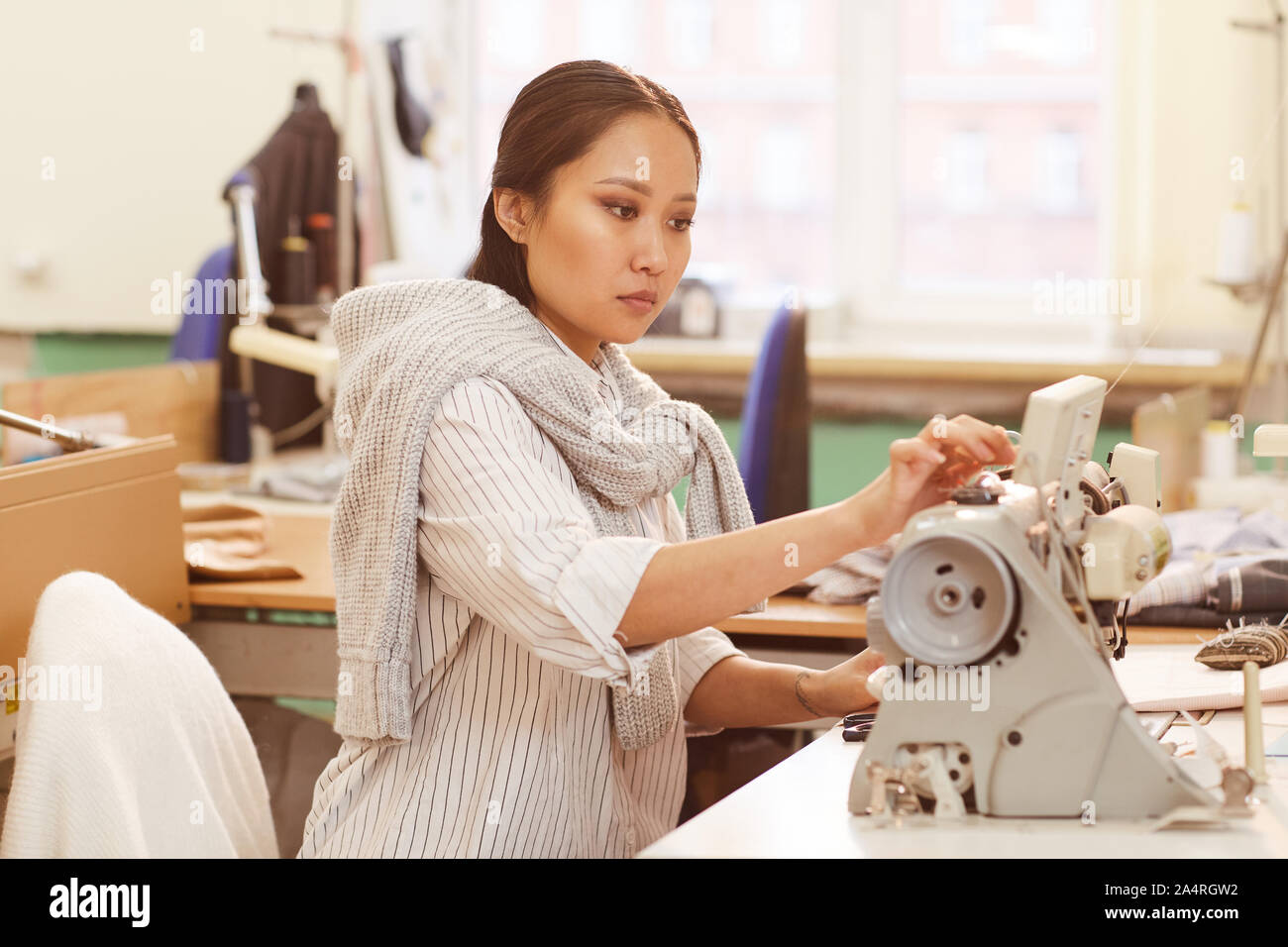 Serious Asian dressmaker examining her sewing machine before working on ...
