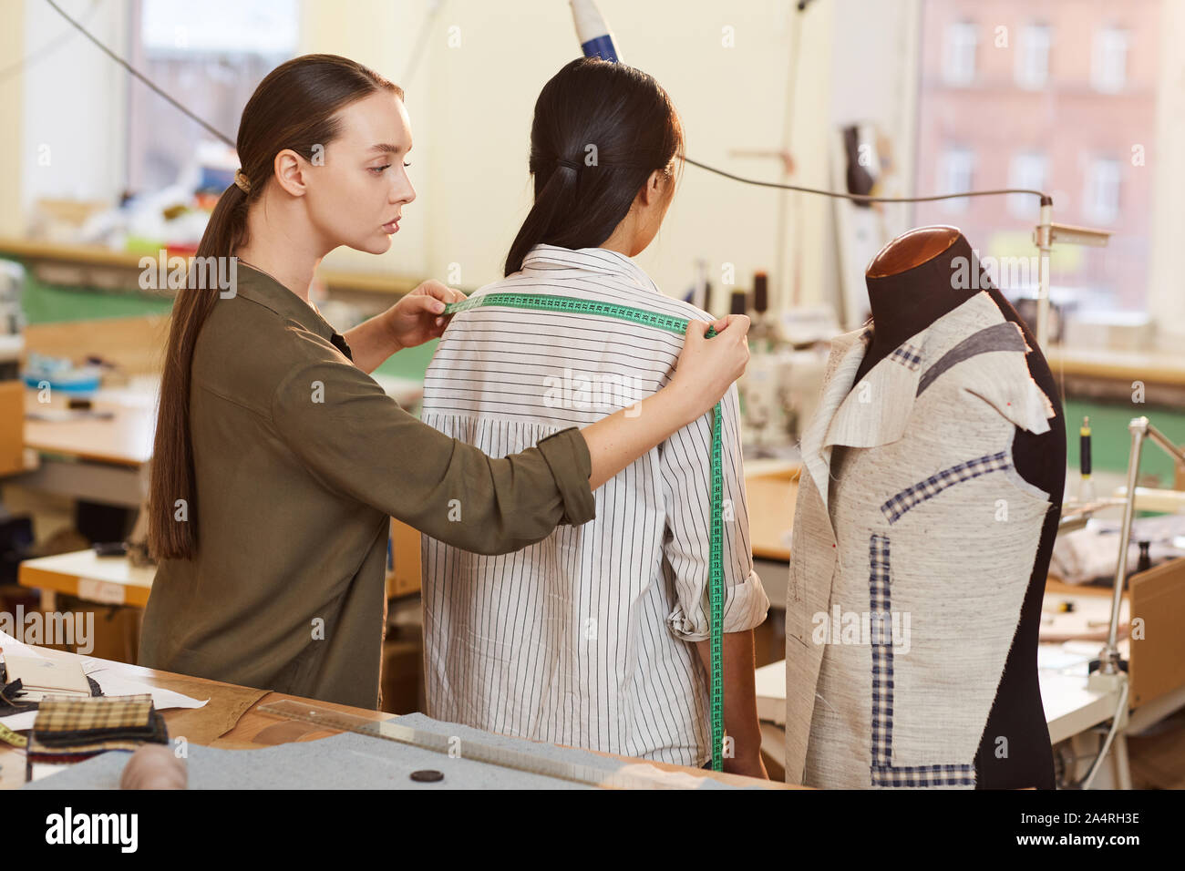 Young tailor measuring length of shoulders with tape measure of her ...
