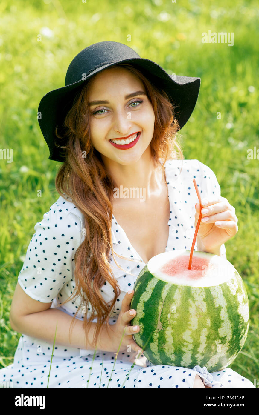 Pretty woman is holding watermelon with cocktail straw on green grass ...