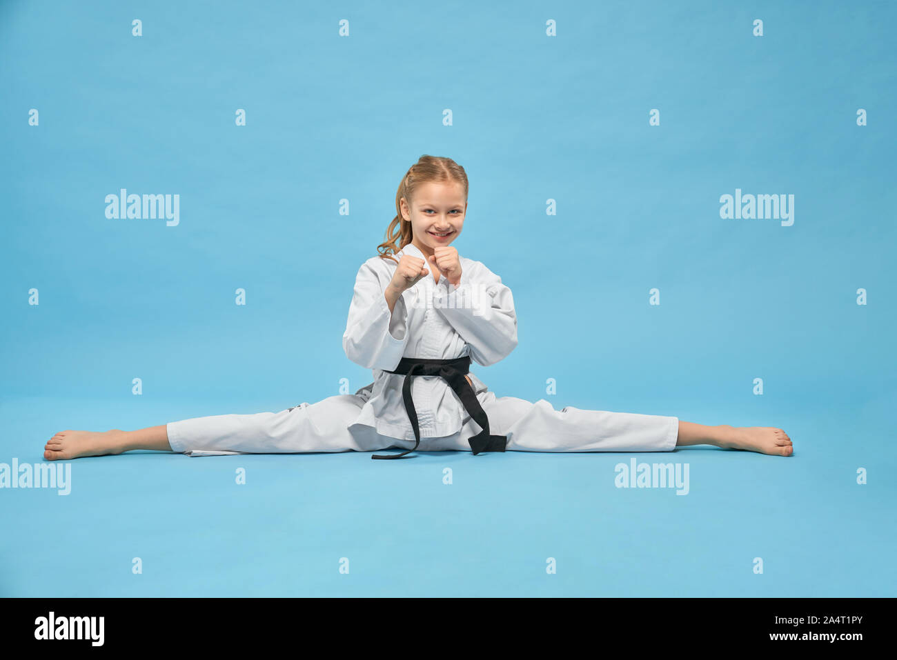Karate girl in white kimono with black belt training, looking at camera ...