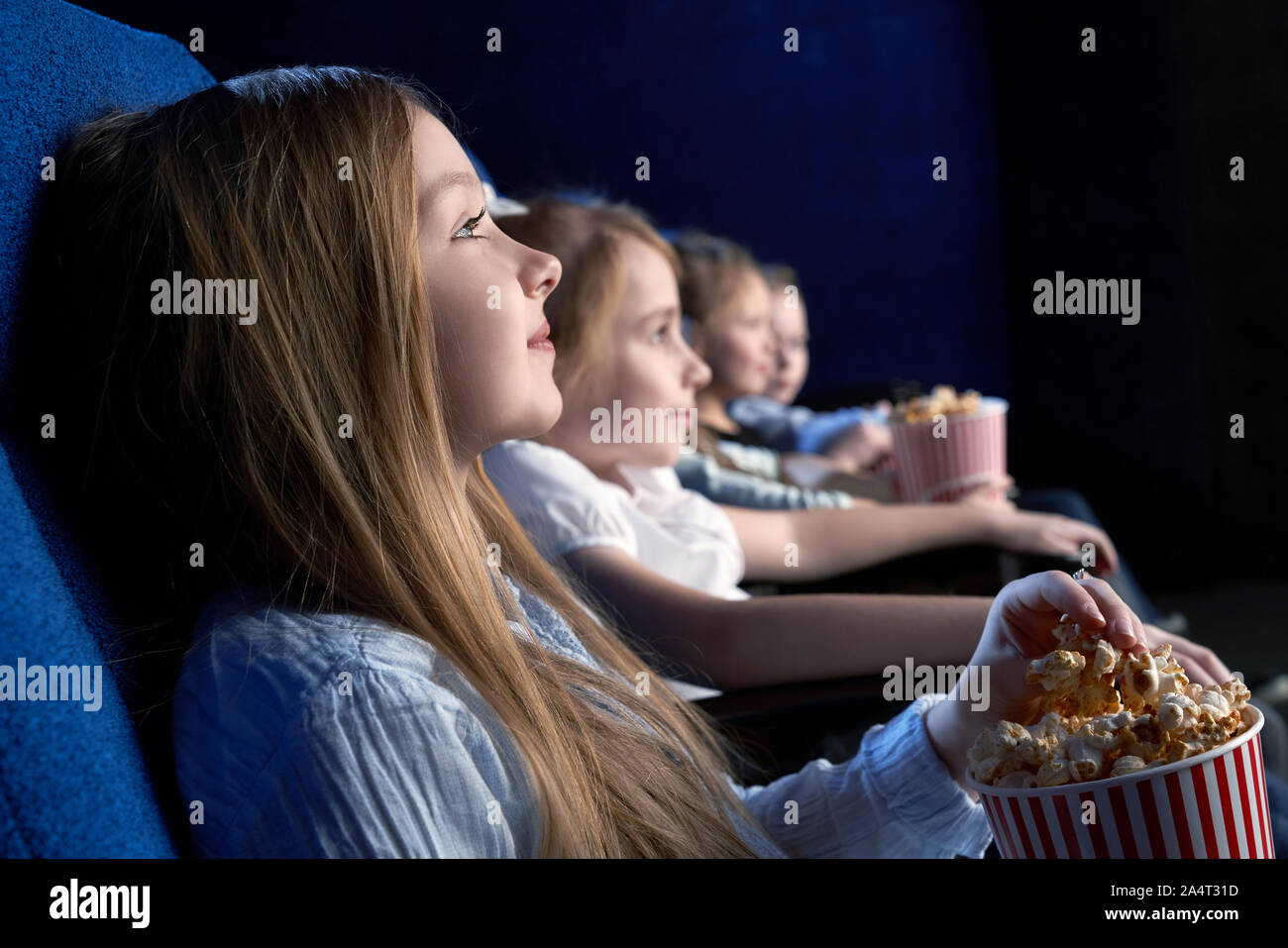 View from side of beautiful little girl sitting in cinema and watching ...