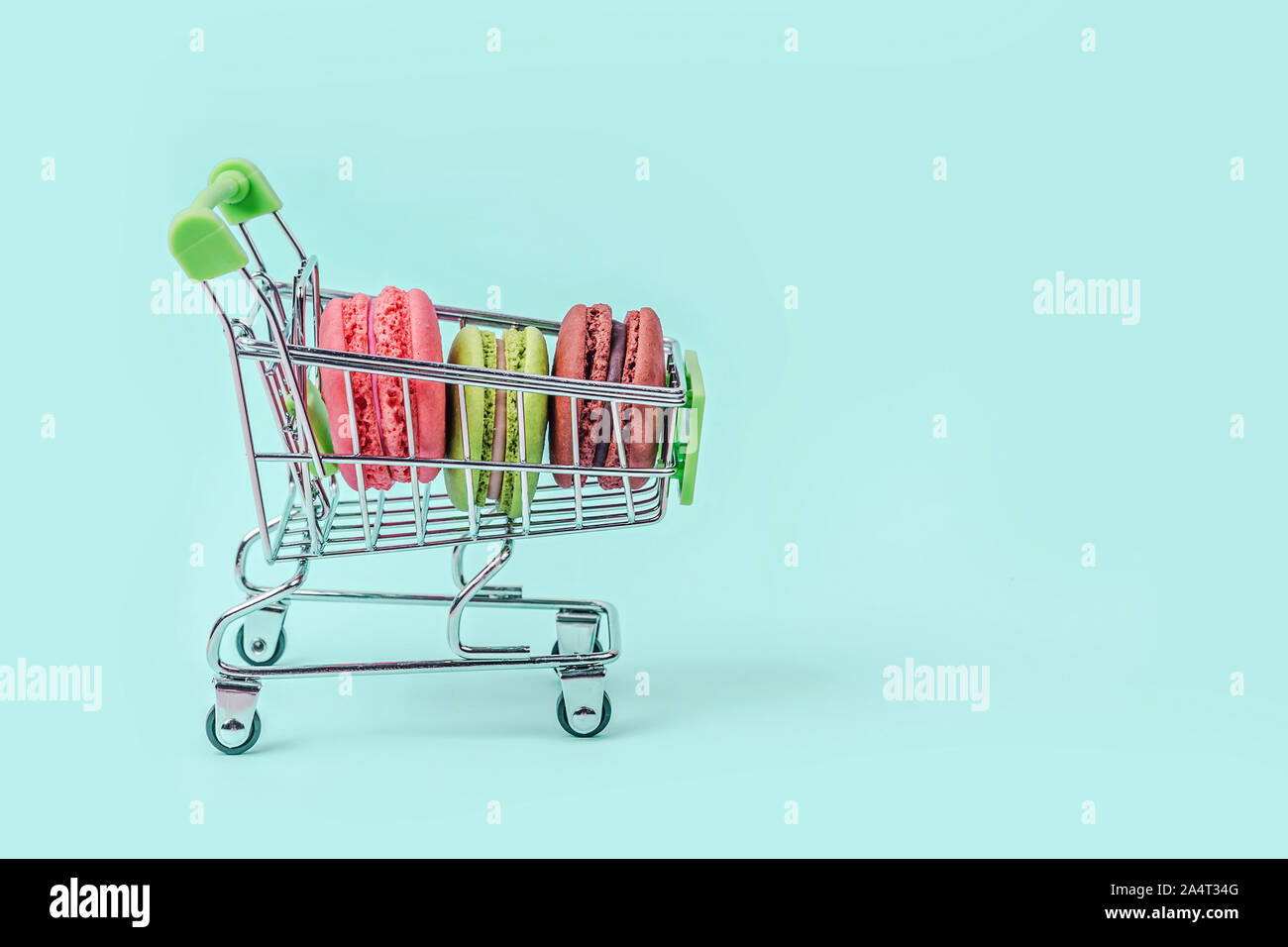 Assorted colorful macaroons in toy shopping cart on mint green ...