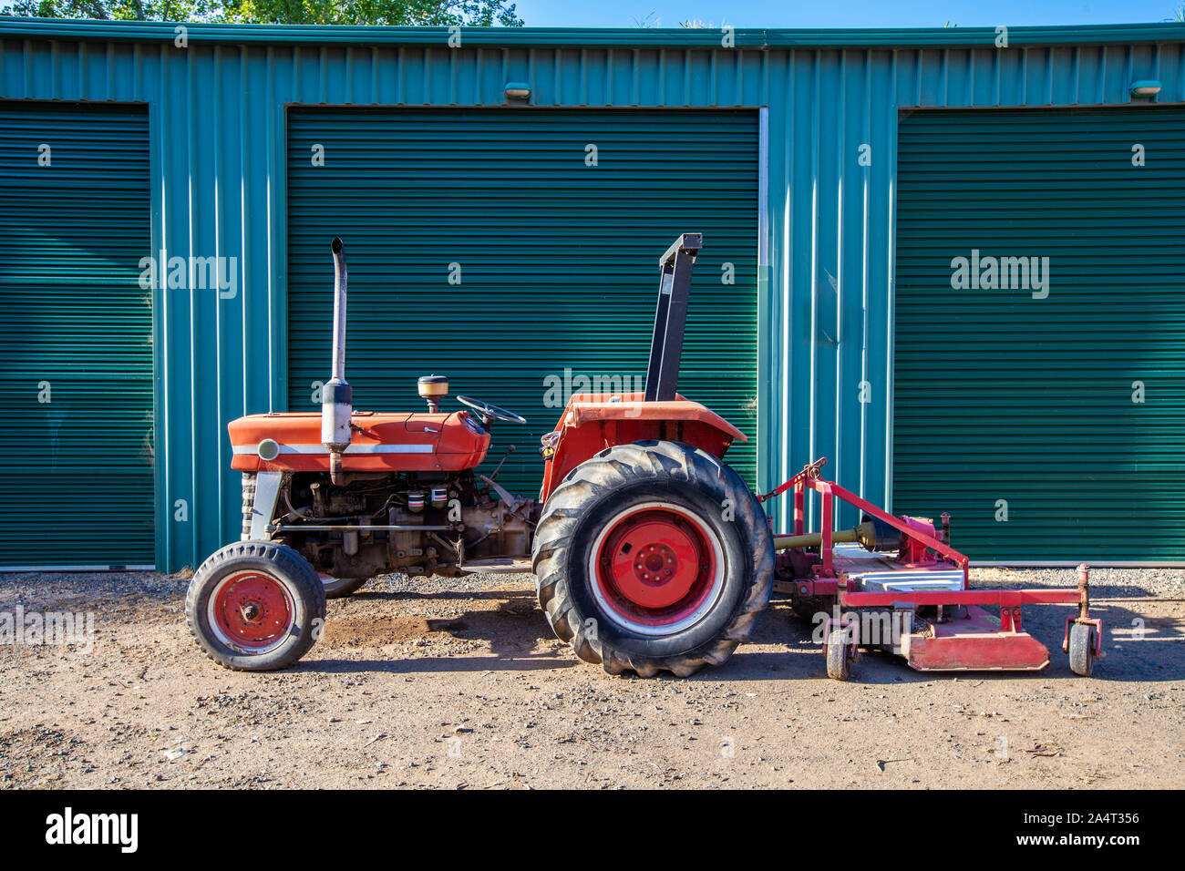 Old tractor with attached lawn mower against warehouse doors in ...