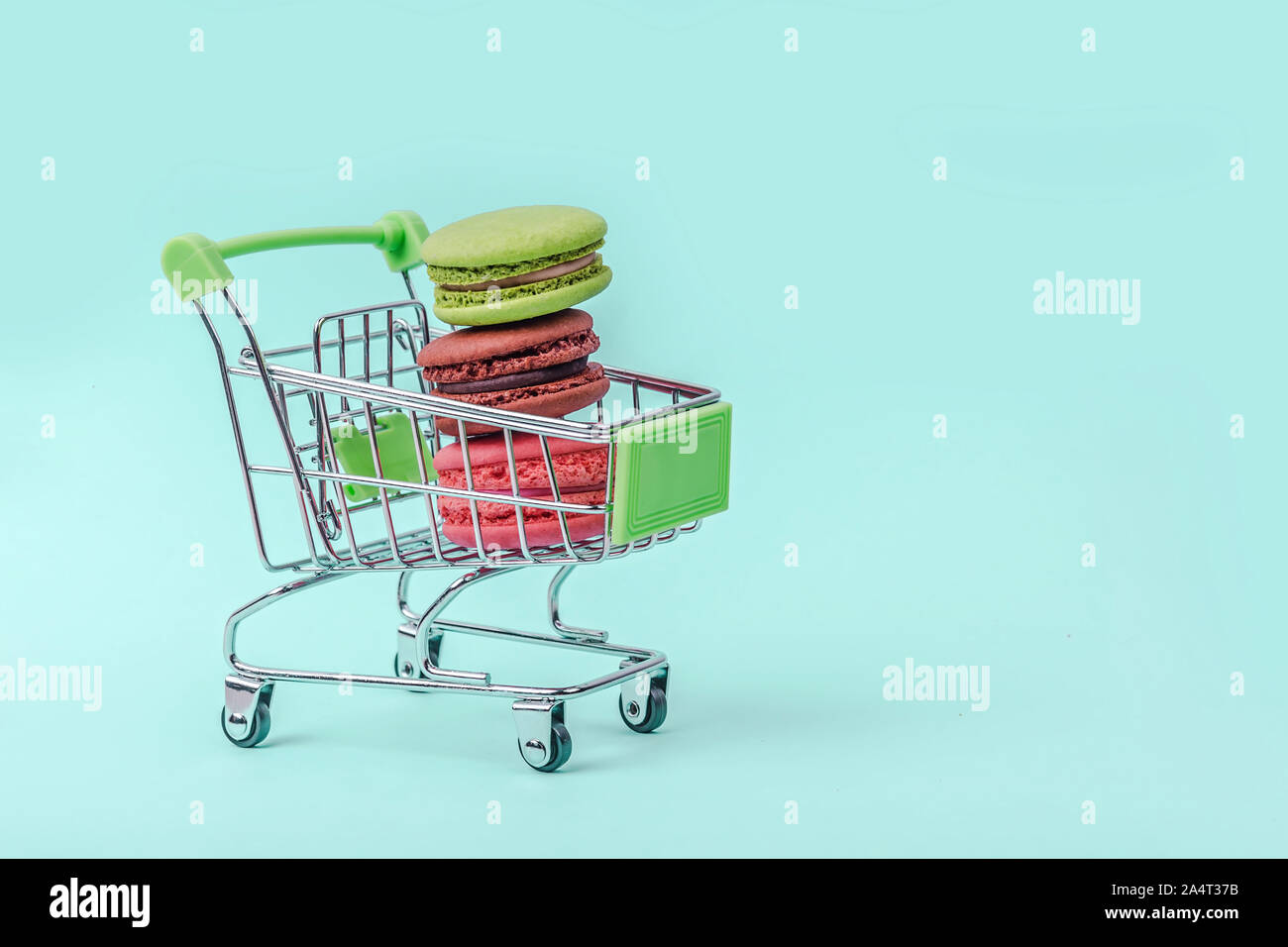 Assorted colorful macaroons in toy shopping cart on mint green ...
