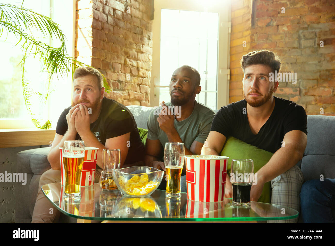 Group of friends watching game on TV at home. Sport fans spending time ...