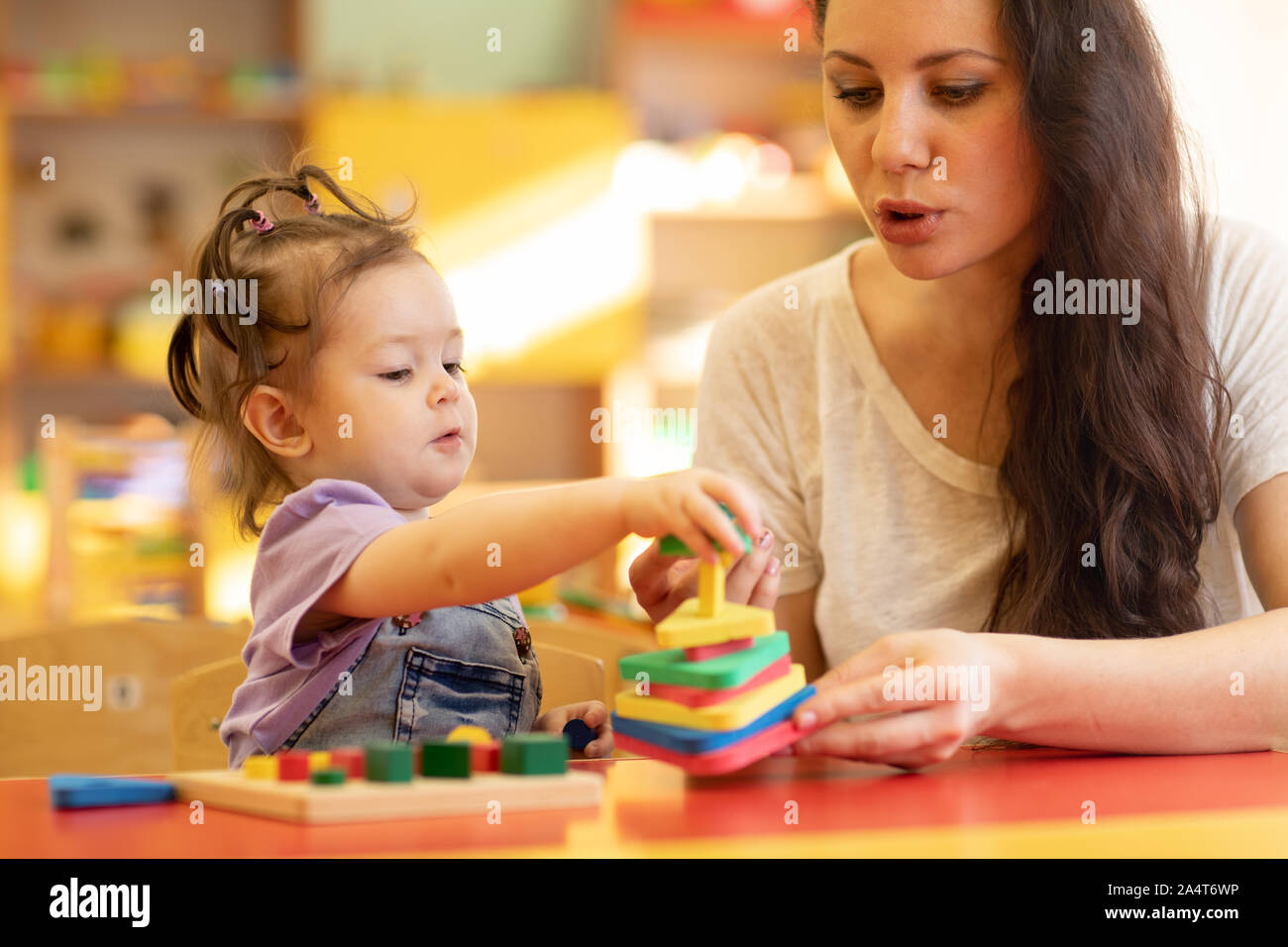 Teacher and kid girl playing colorful block toys in creche Stock Photo ...