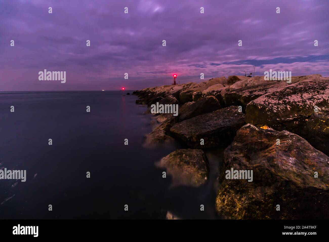 Red lighthouse at night with the light on the dam on the sea Stock ...