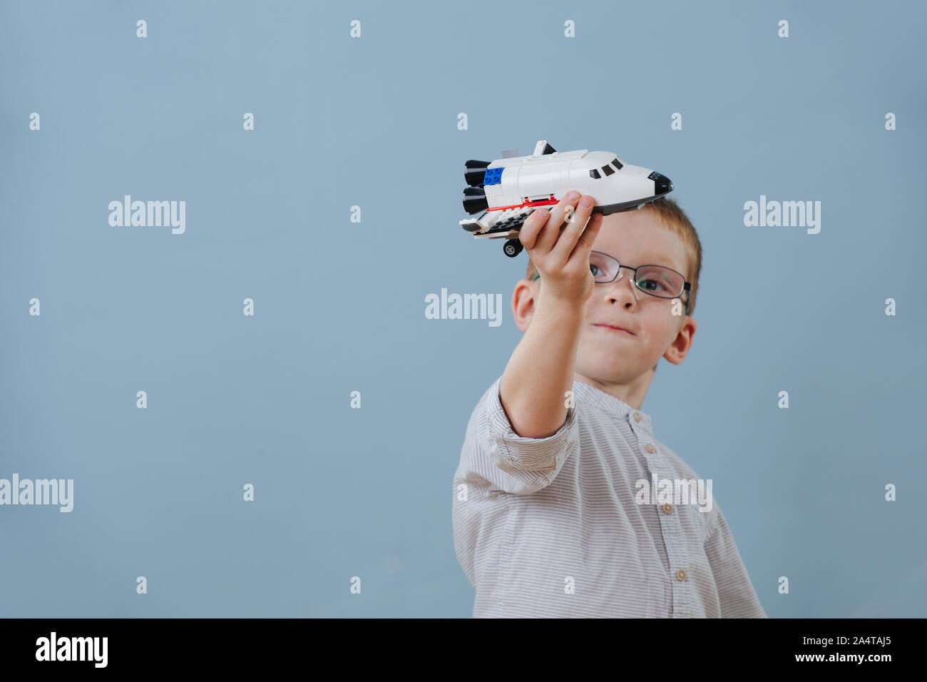 Little ginger boy in glasses plays with space shuttle model over blue ...