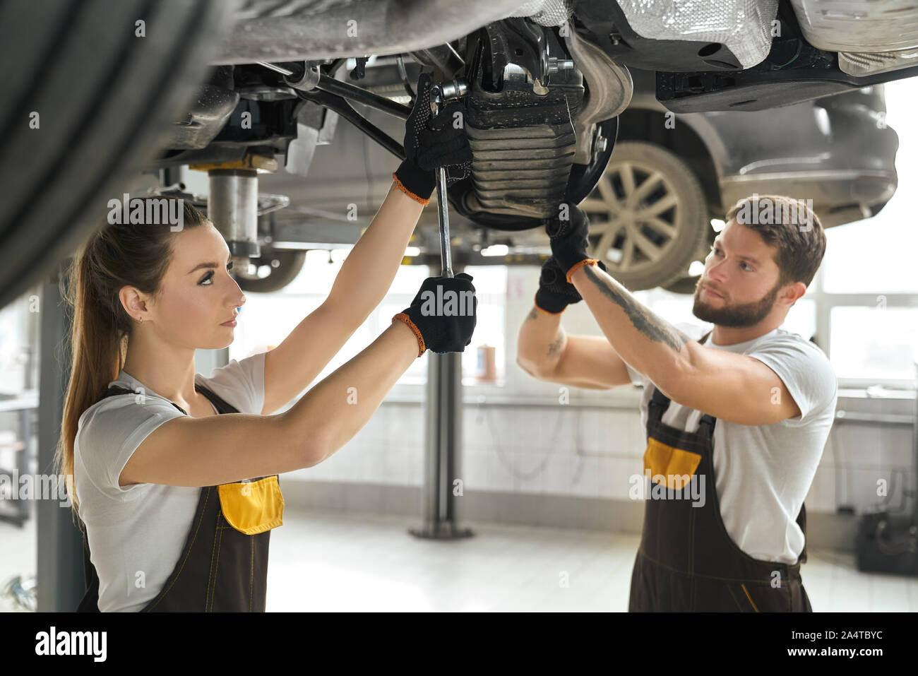 Young woman and man working together with undercarriage of automobile ...