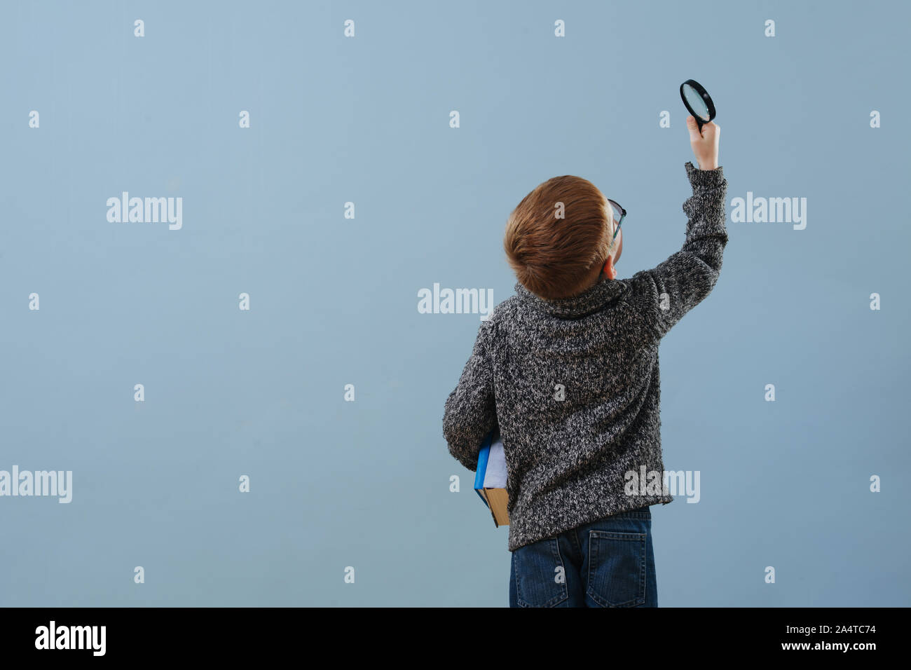 Curious ginger boy in glasses looking up through magnifying glass over ...