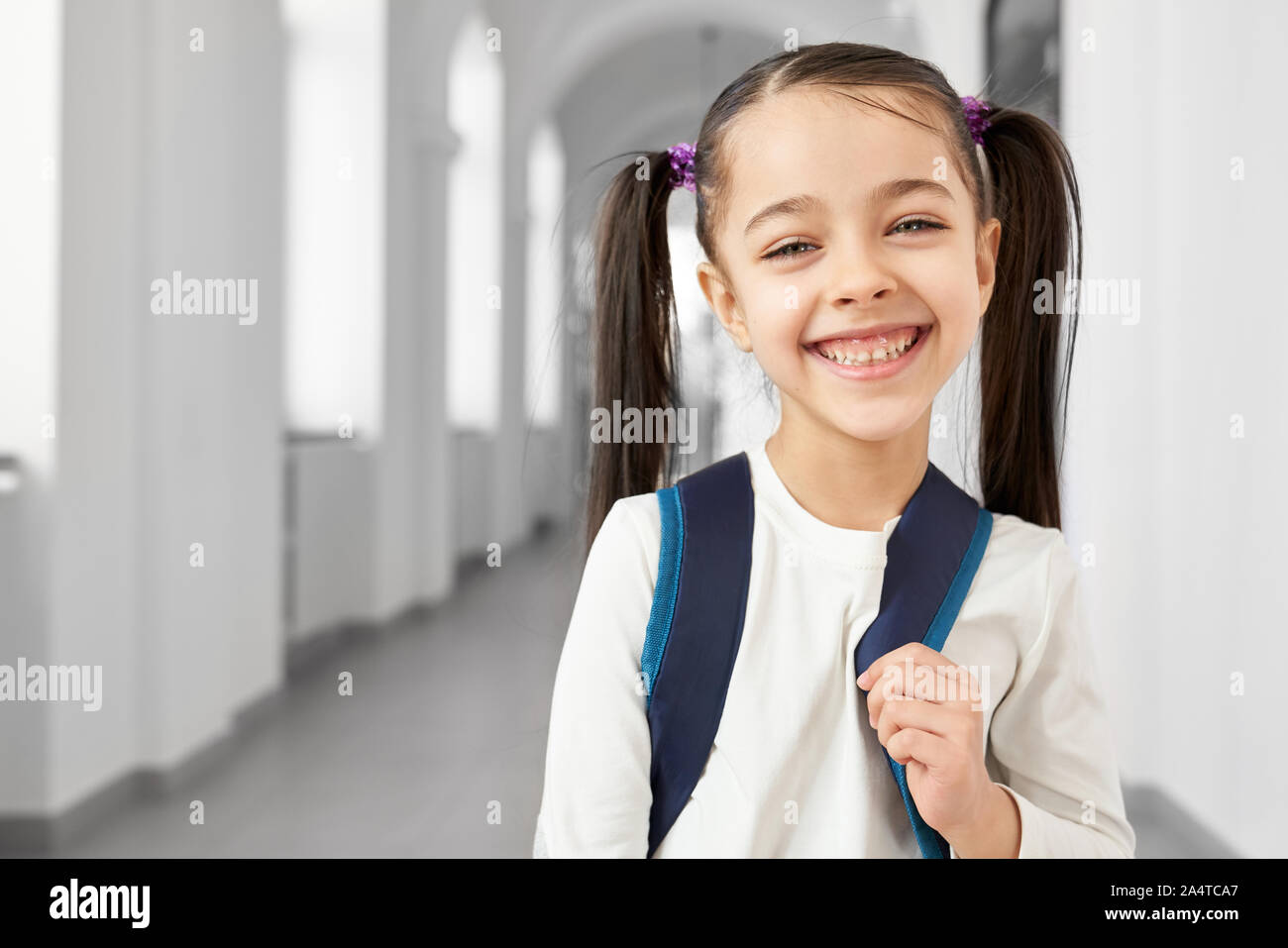 Cute, pretty, happy schoolgirl with hair tails standing in long, light ...
