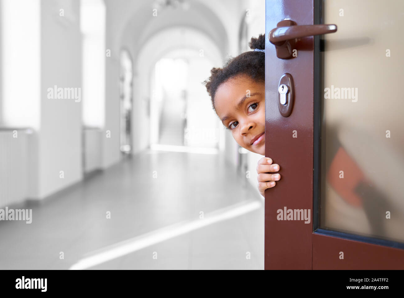 Pretty African girl hiding from opened door in school corridor ...