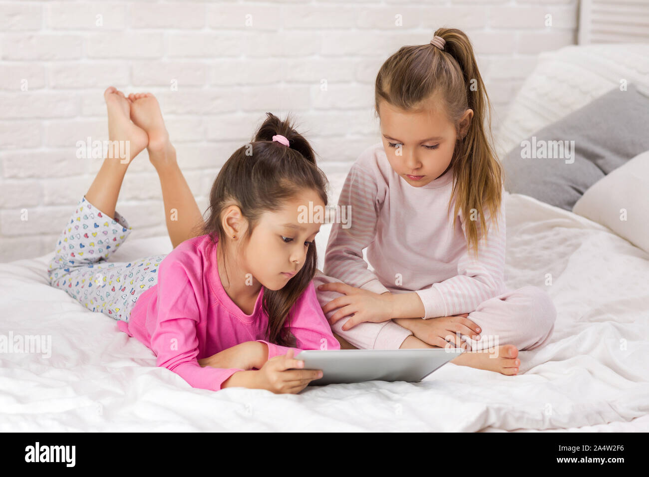 two cute children girls use digital tablet in bed. child playing on ...