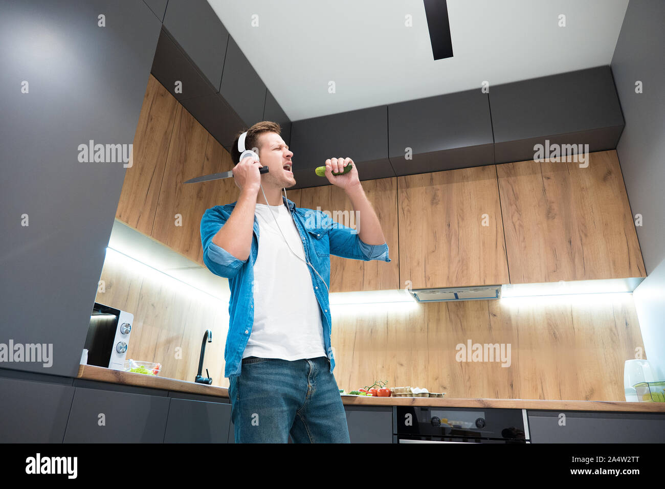 young handsome man in headphones dancing while cooking in the kitchen ...