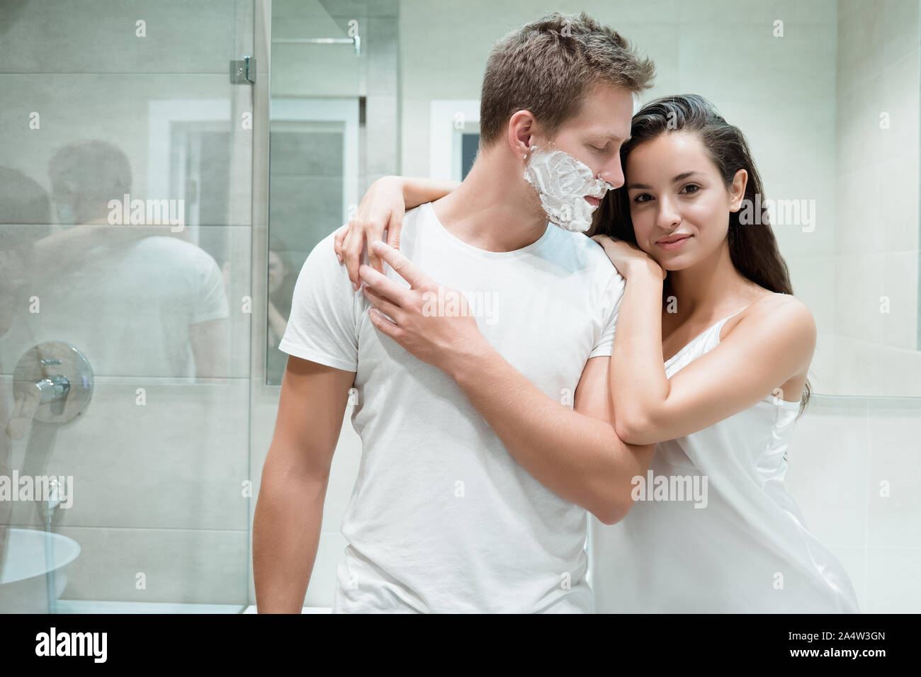 young couple handsome man and beautiful woman hugging in bathroom while ...