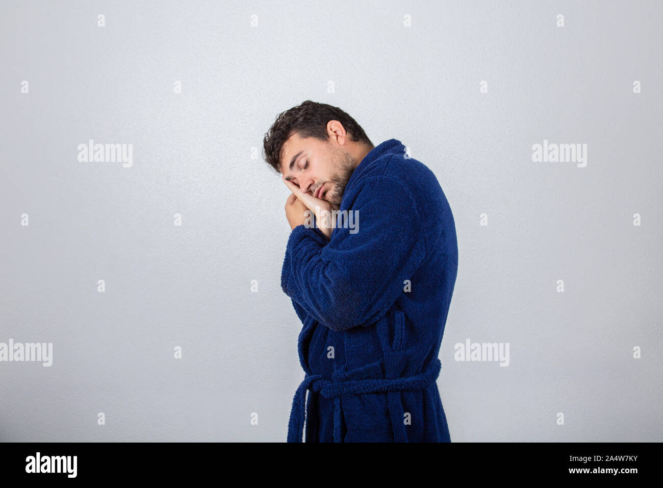 Portrait of sleepy young man wearing blue bathrobe holding hand to ...