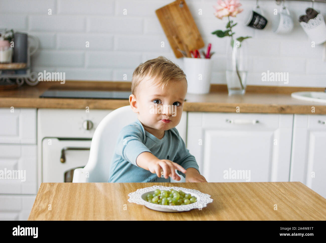 Charming little baby boy eating first food green grape at the bright ...