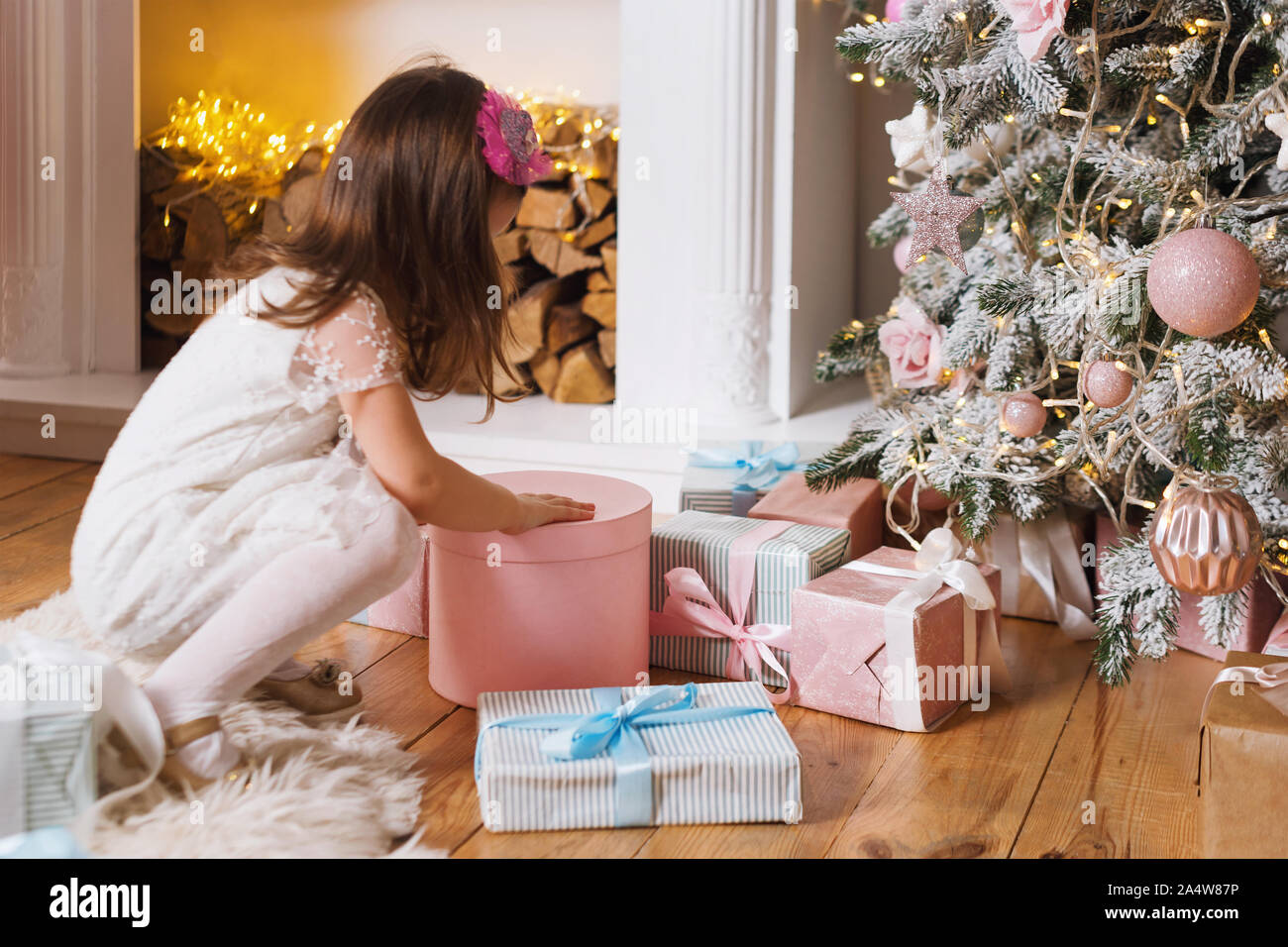 Little girl opening a Christmas gift, Christmas tree and fireplace on ...