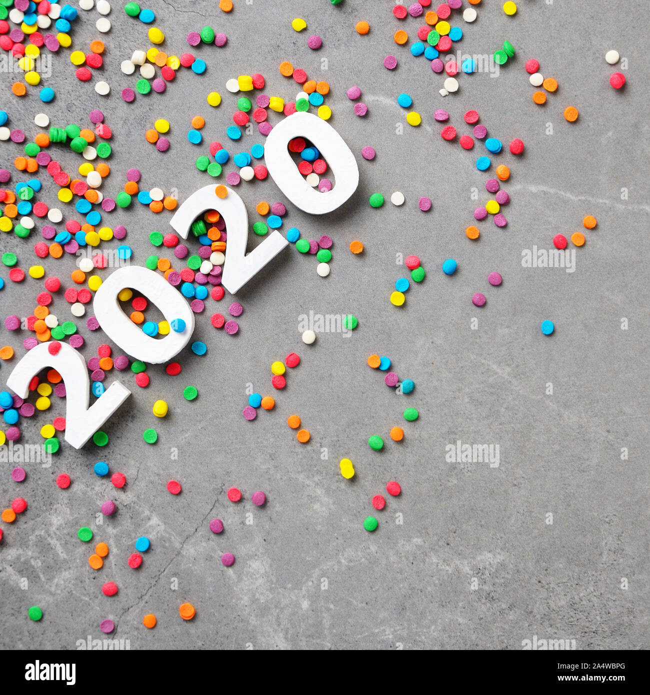 Flat lay view at numbers 2020 with color sugar sprinkles on stone table ...