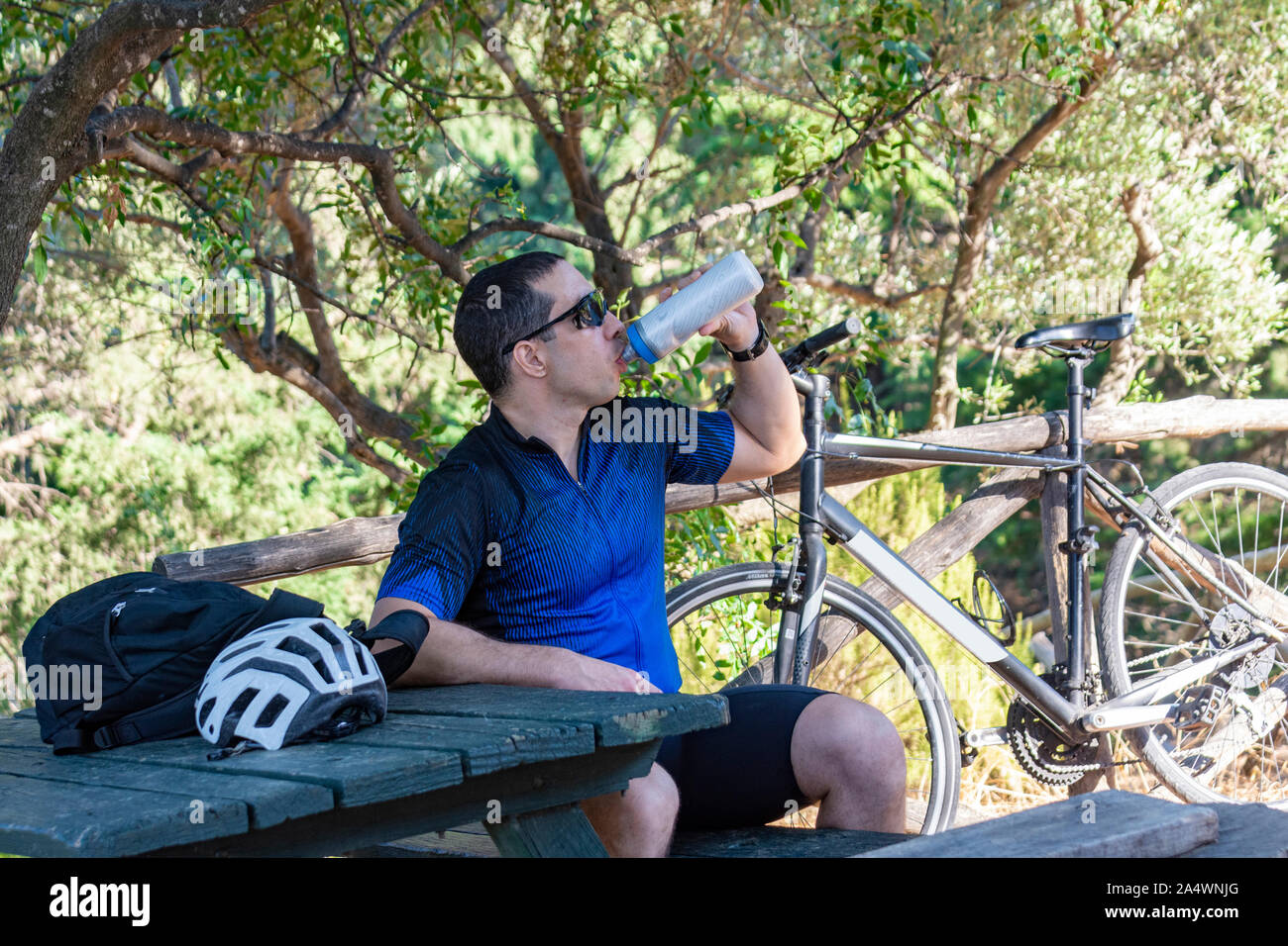 male cyclist resting and drinking isotonic drink after training with ...