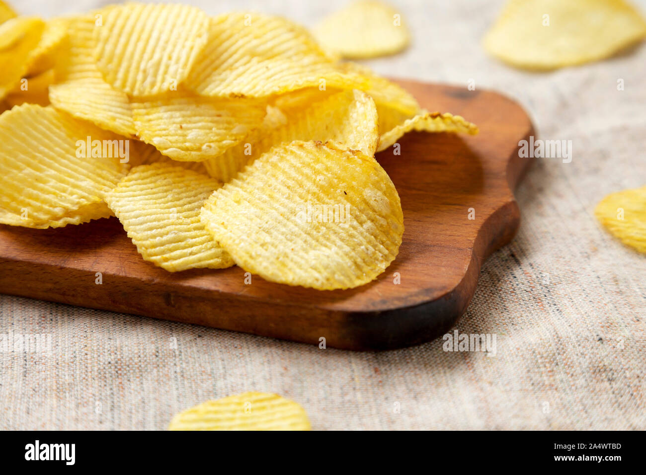 Salted wavy potato chips on a rustic wooden board, side view. Close-up ...