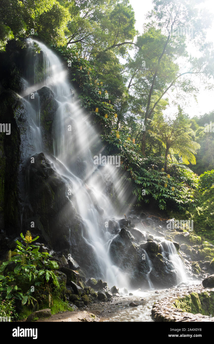 Waterfall with bright sun rays bursting through the mist created by the ...