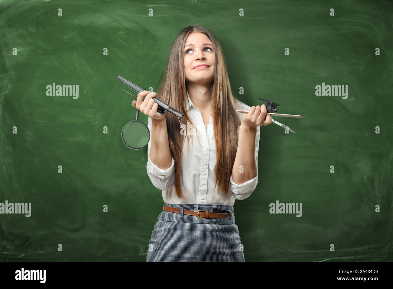 Confused businesswoman on green chalkboard background holding pens ...