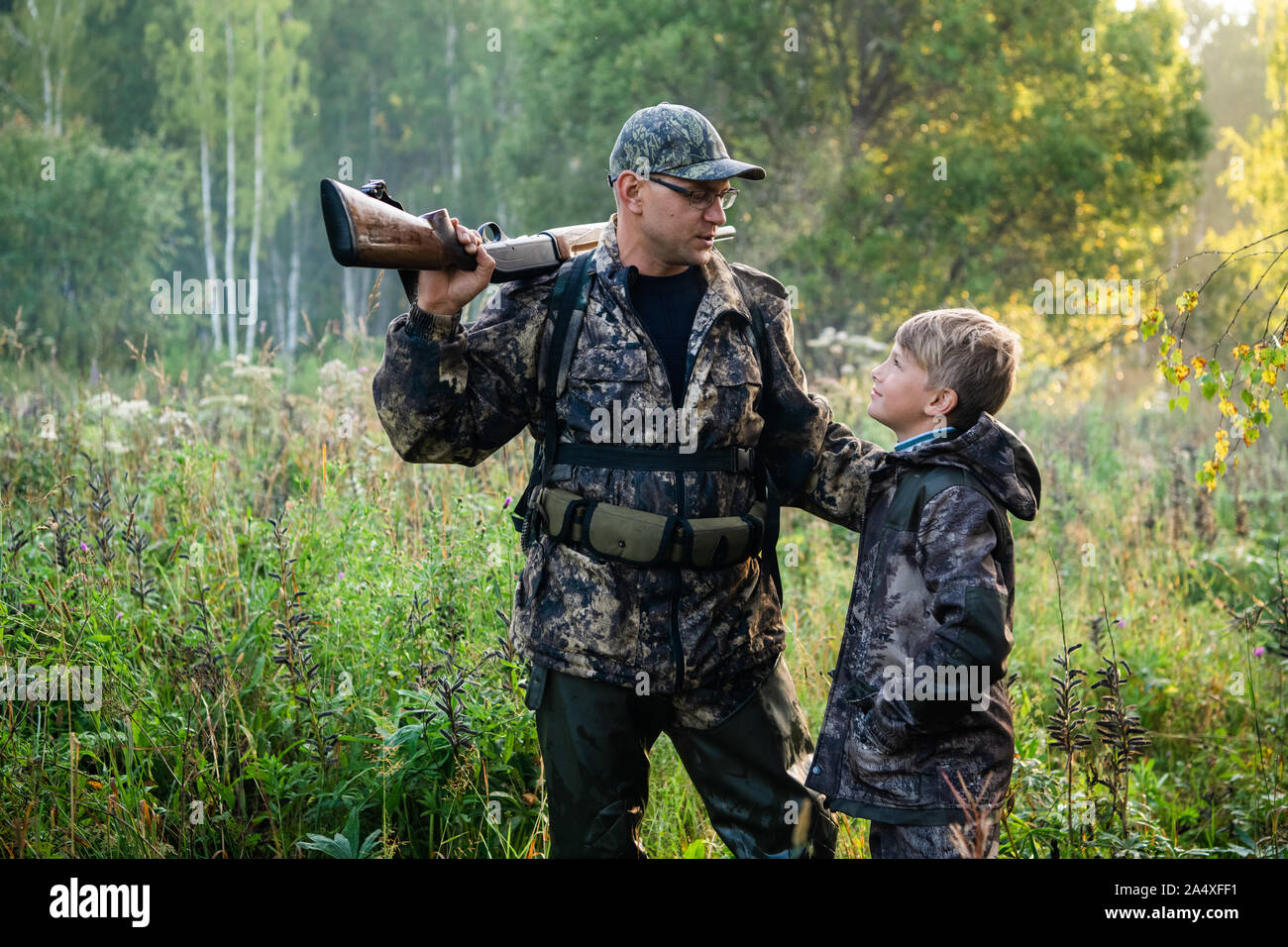 Father with gun showing something to son while hunting on a nature ...