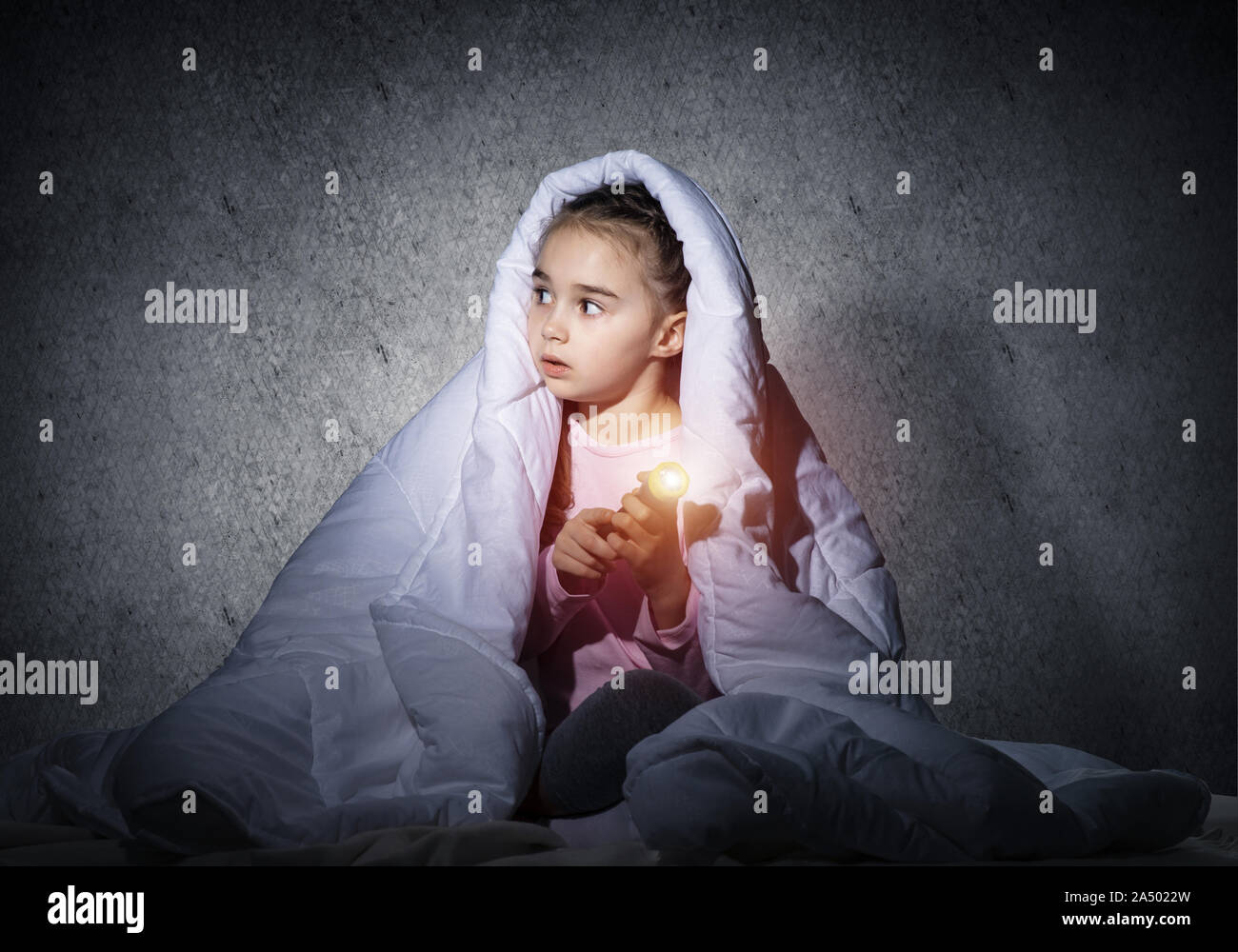 Frightened girl with flashlight hiding under blanket. Scared kid lying ...