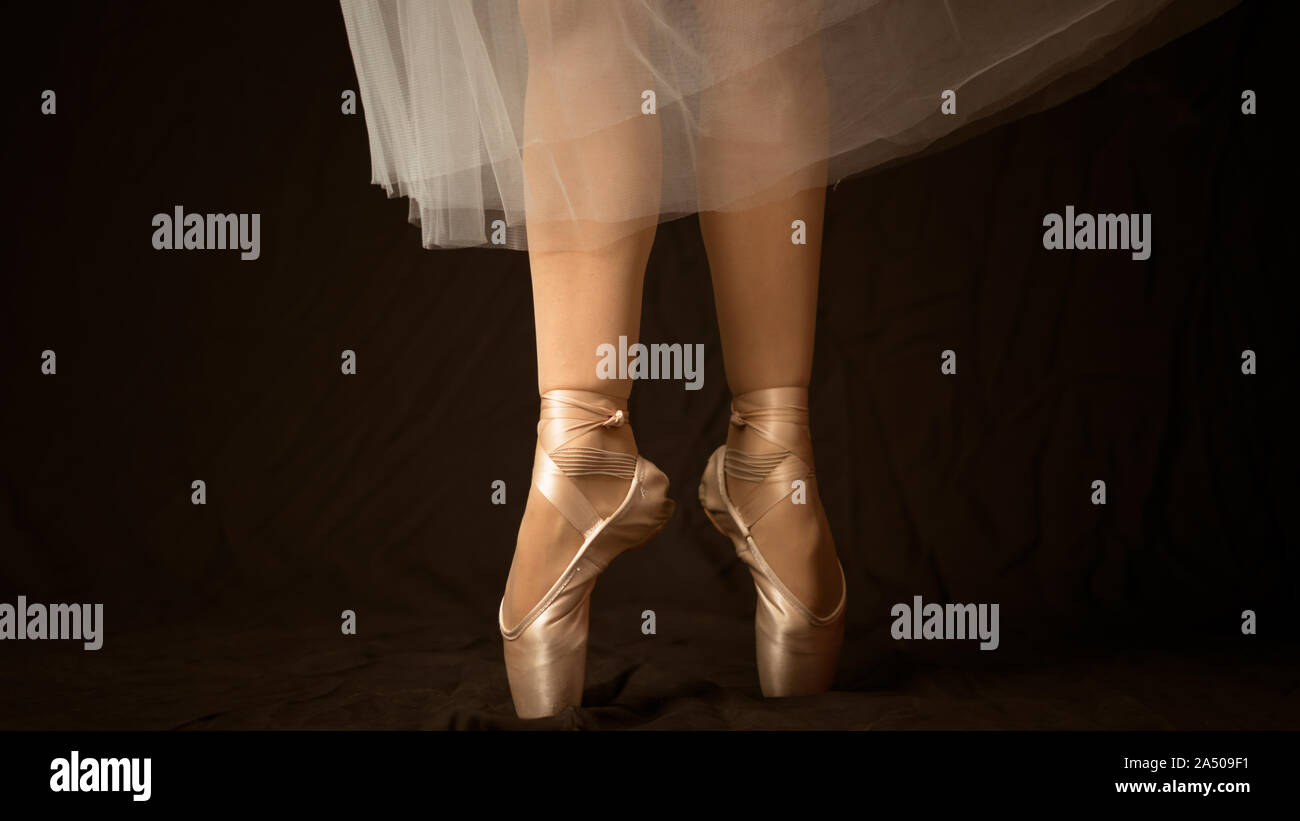 Close-up of dancing legs of ballerina wearing white pointe on a black ...