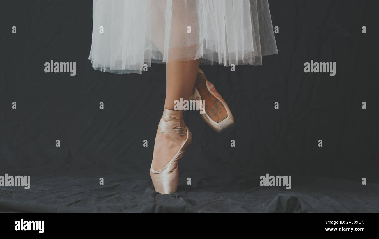 Close-up of dancing legs of ballerina wearing white pointe on a black ...
