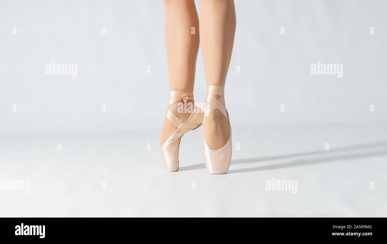 Close-up of dancing legs of ballerina wearing white pointe on a white ...