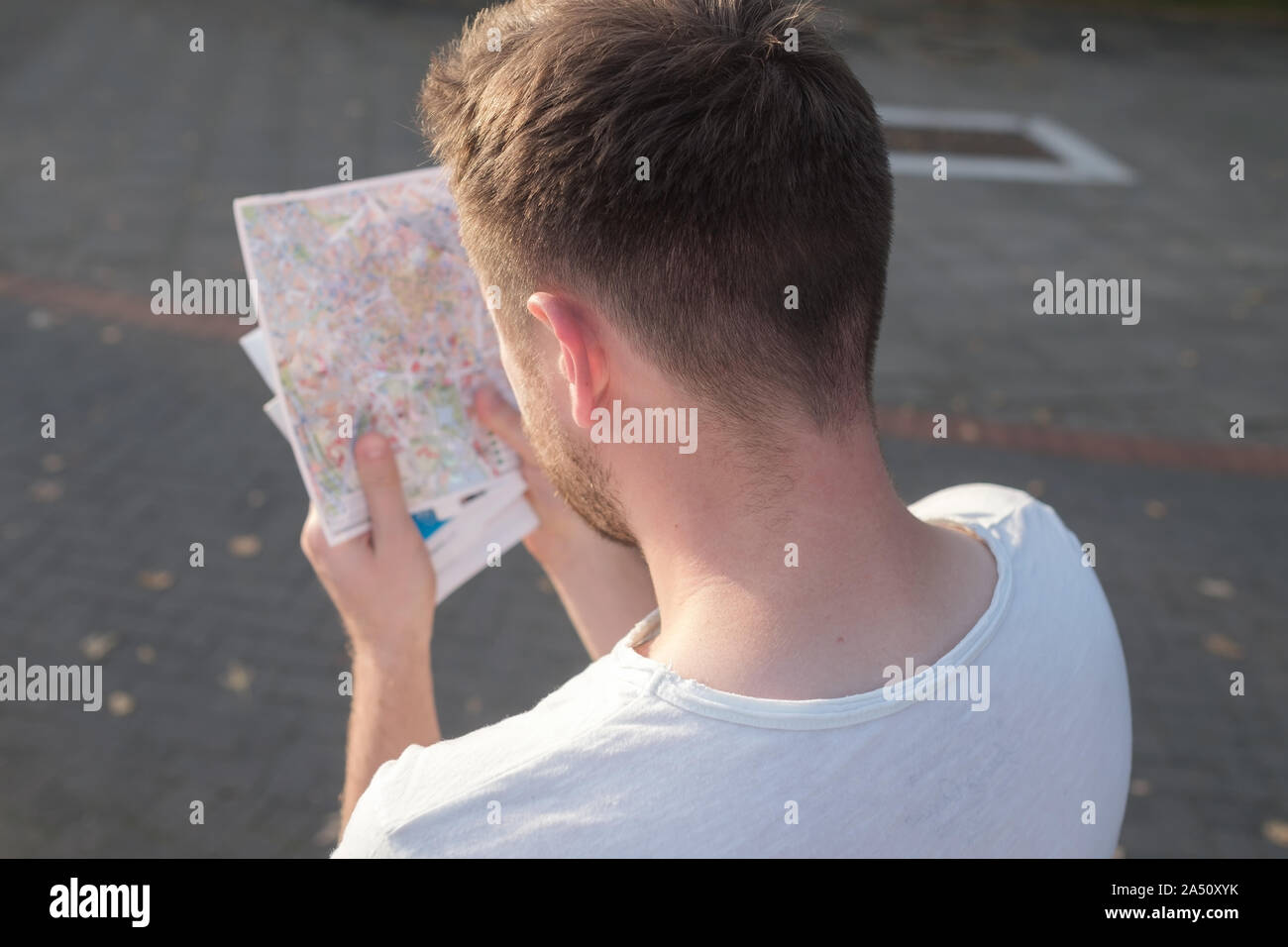 Caucasian young man tourist on the street looking at a guide being lost ...