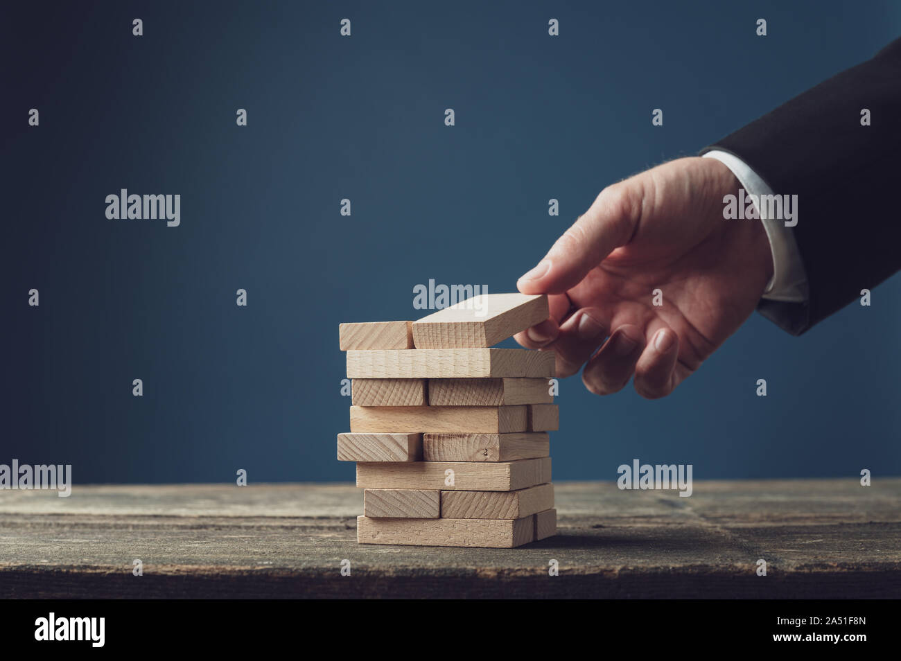 Hand of a businessman making a stack of wooden pegs on rustic wooden ...