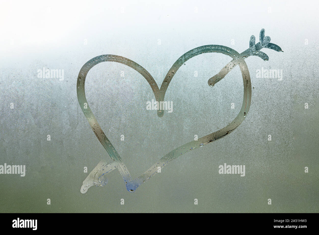 Love heart with arrow on a wet window. Closeup on foggy glass ...