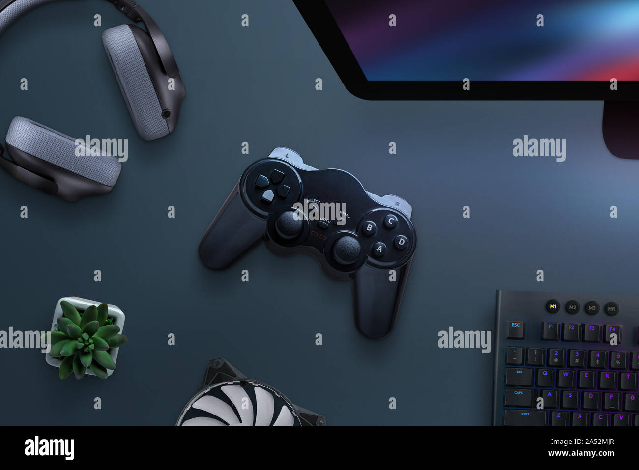 Joypad on desk surrounded with headphones, cooler, keyboard and ...