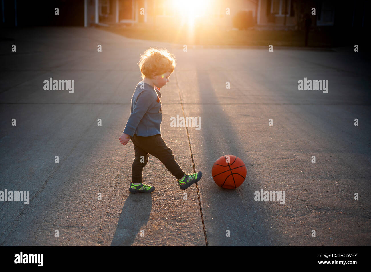 Toddler boy kicking basketball outdoors in street in pretty light Stock ...