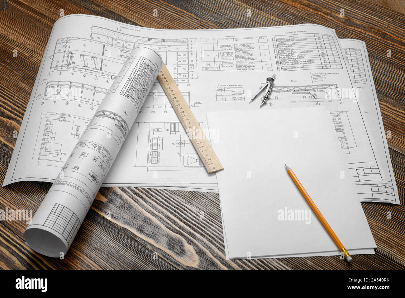 A set of open and rolled up blueprints on wooden table background with ...